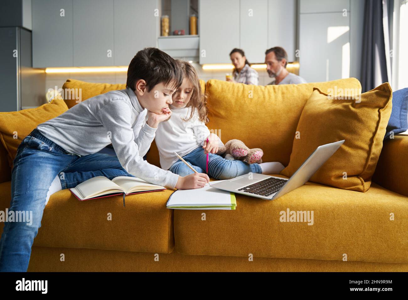 Kids writing in notepad before laptop on sofa Stock Photo - Alamy