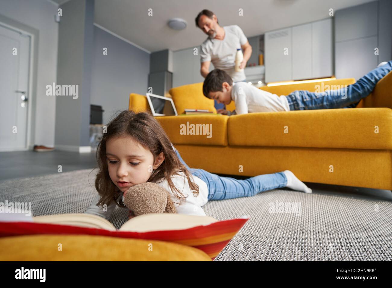Attentive child reading book on floor before sofa Stock Photo - Alamy