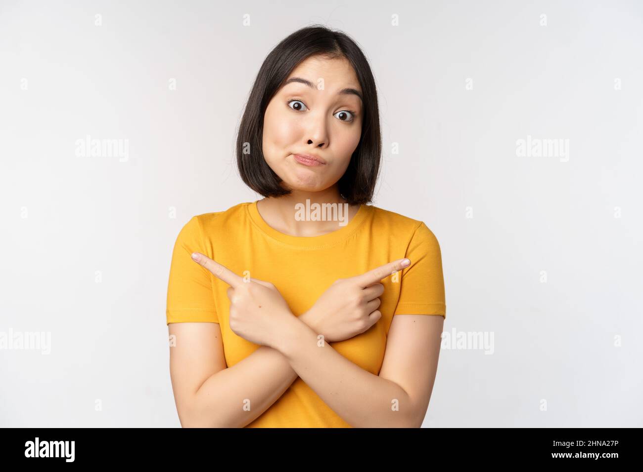 Complicated asian girl pointing fingers sideways, showing left and right choices, staring ...