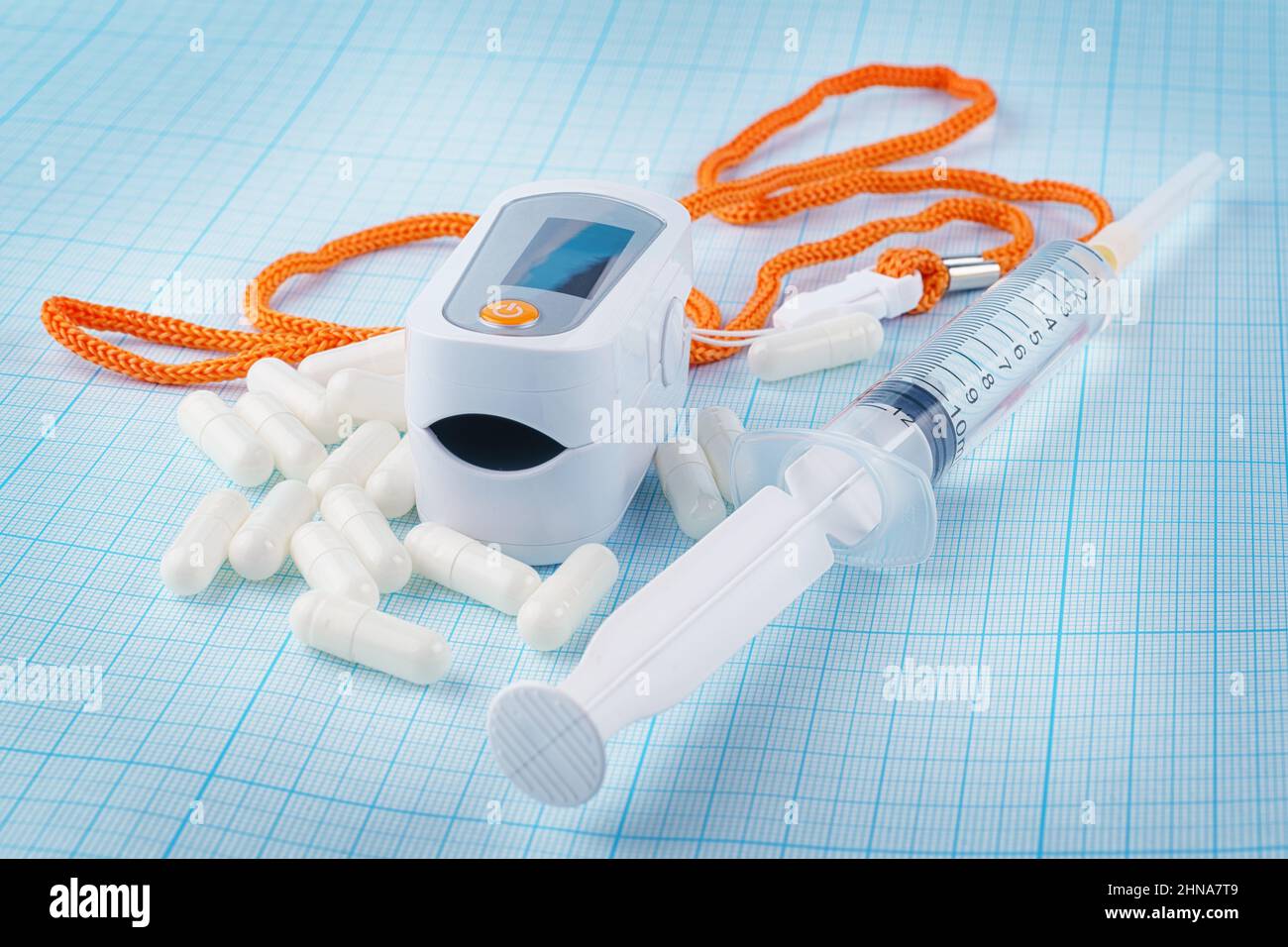 White pulse oximeter, capsules and syringe on graph paper background ...