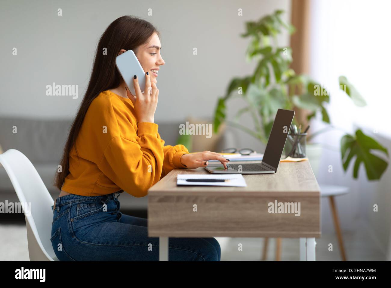 Young Caucasian woman using laptop and speaking on smartphone, working ...