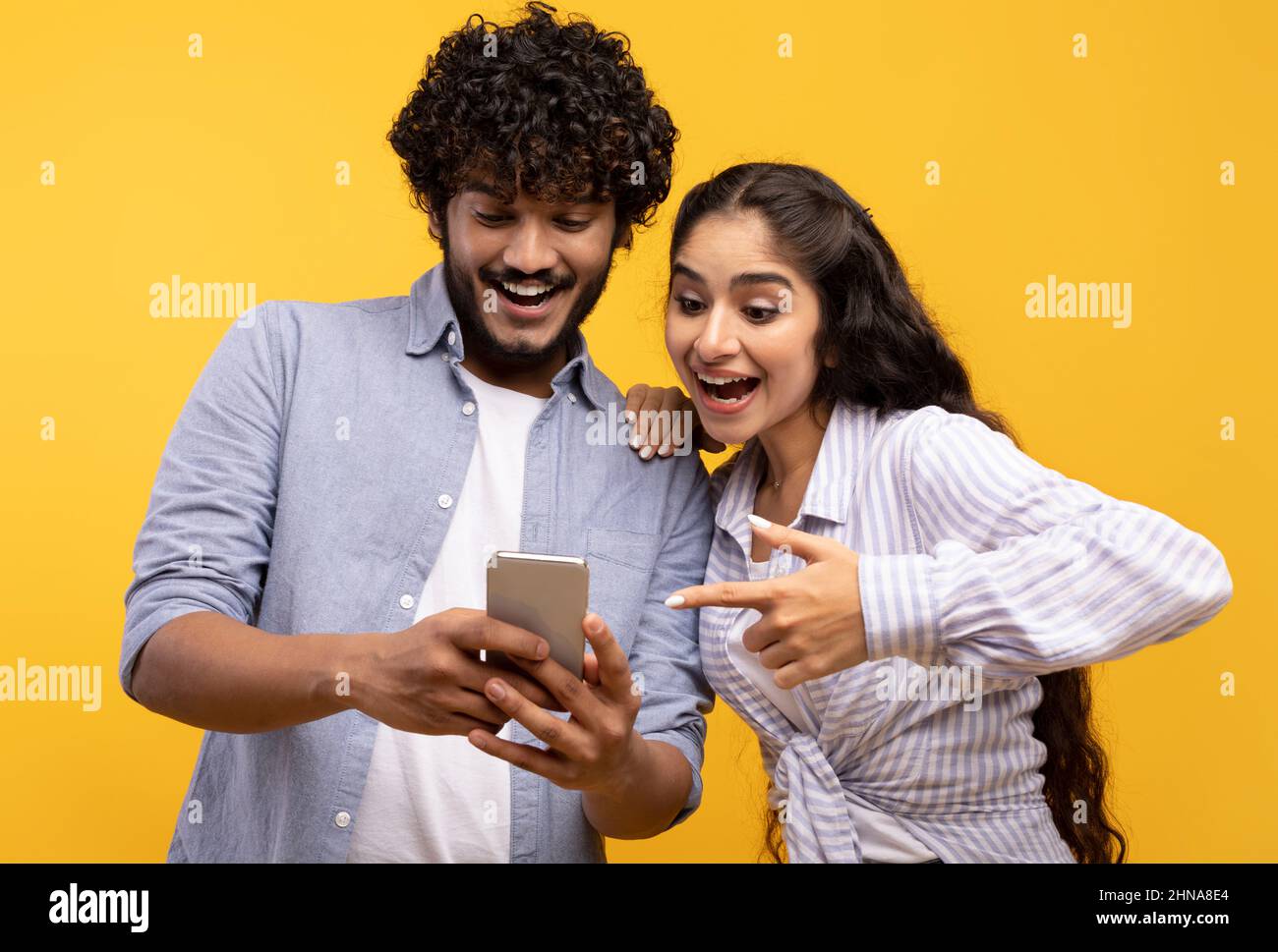 Excited indian couple using cellphone and pointing on it, looking at ...