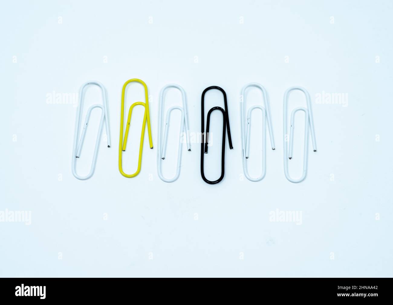 A line of six white, yellow and black paper clips on a plain white ...
