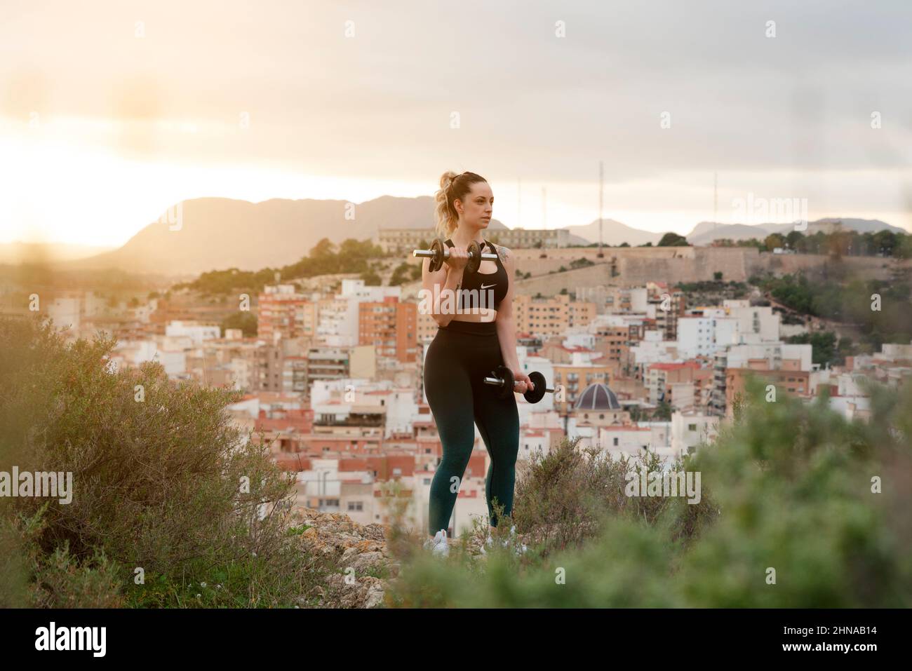 Young fitness woman lifts weights outdoors at sunset Stock Photo - Alamy