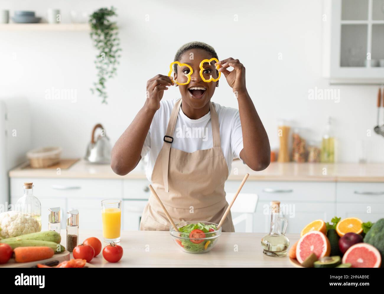 Glad young black female in apron have fun, make salad, puts pieces of ...