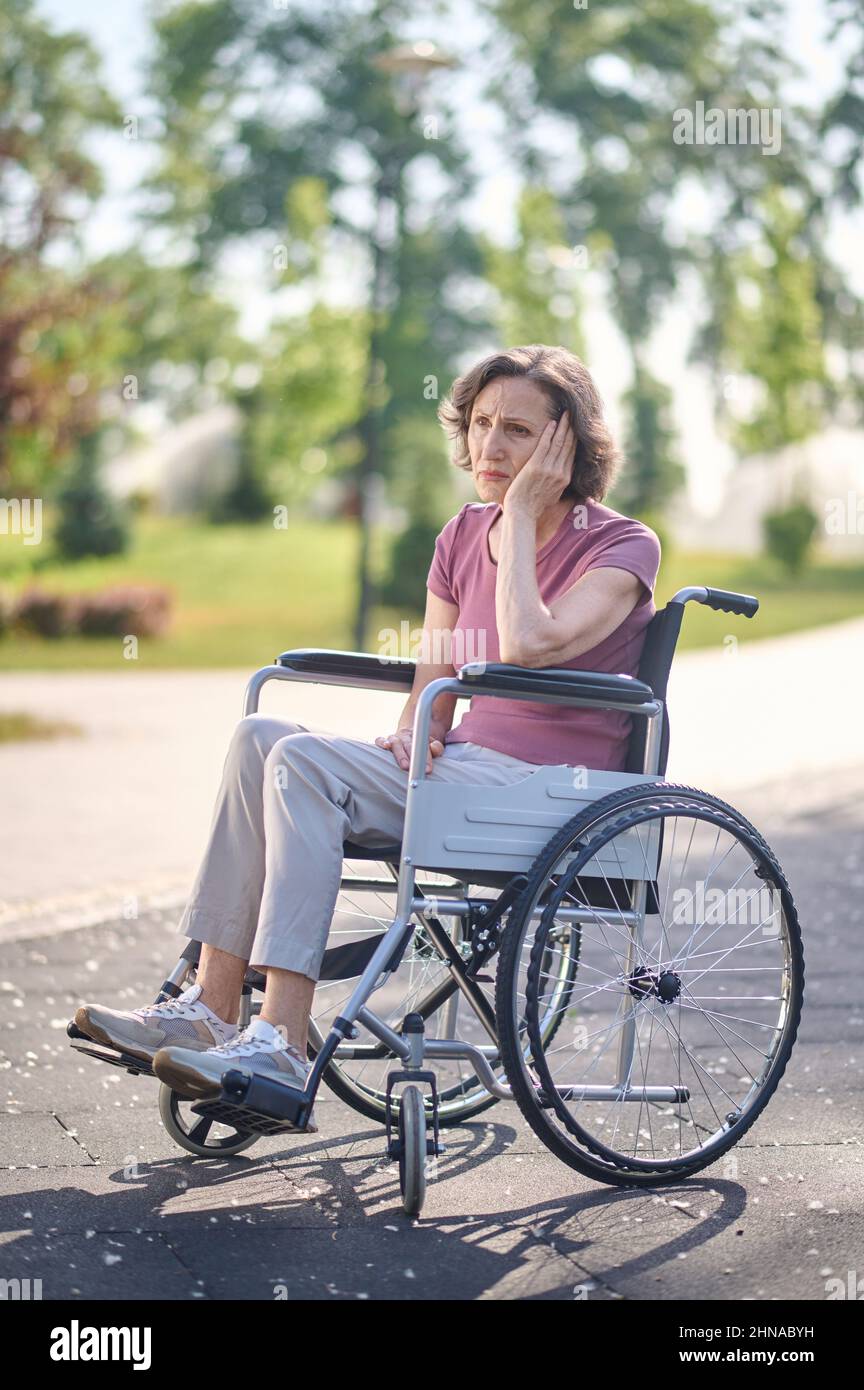Disabled mid aged woman sitting in a wheel-chair with an unhappy look ...
