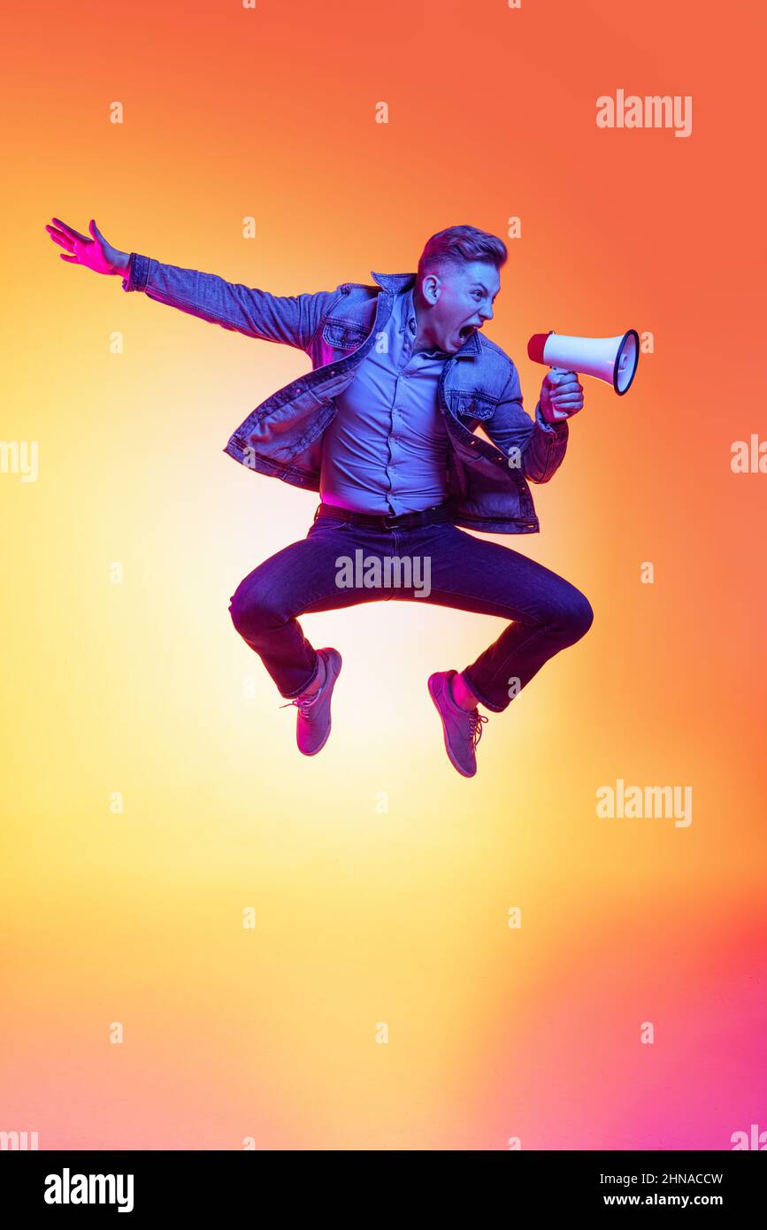 Full-length portrait of young excited man jumping with megaphone ...
