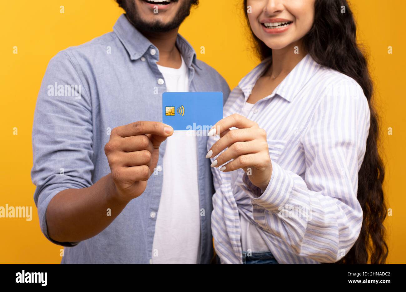 Cropped view of indian couple holding credit card on yellow studio ...