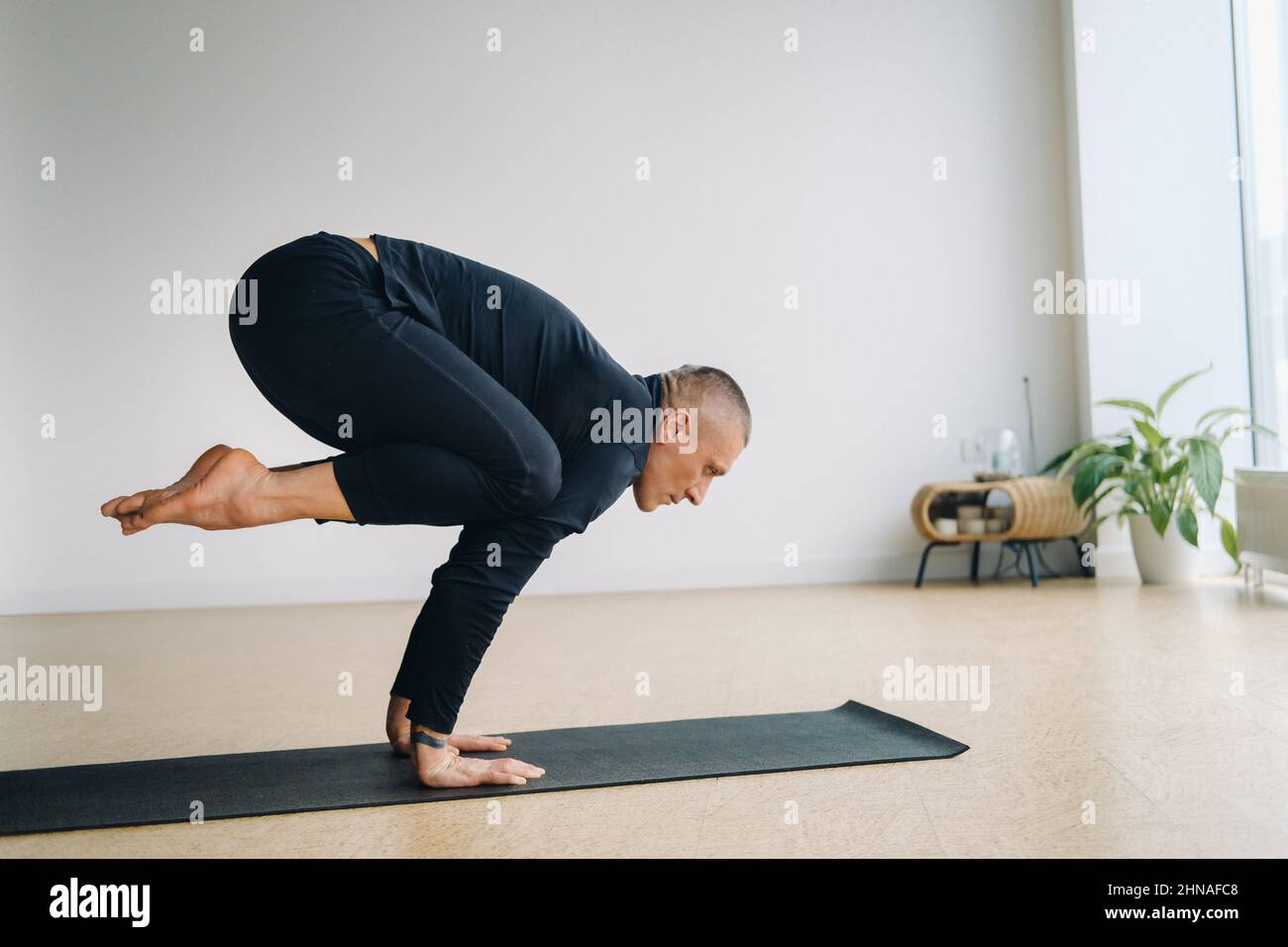 A man in black sportswear does yoga standing on his hands, stretching ...
