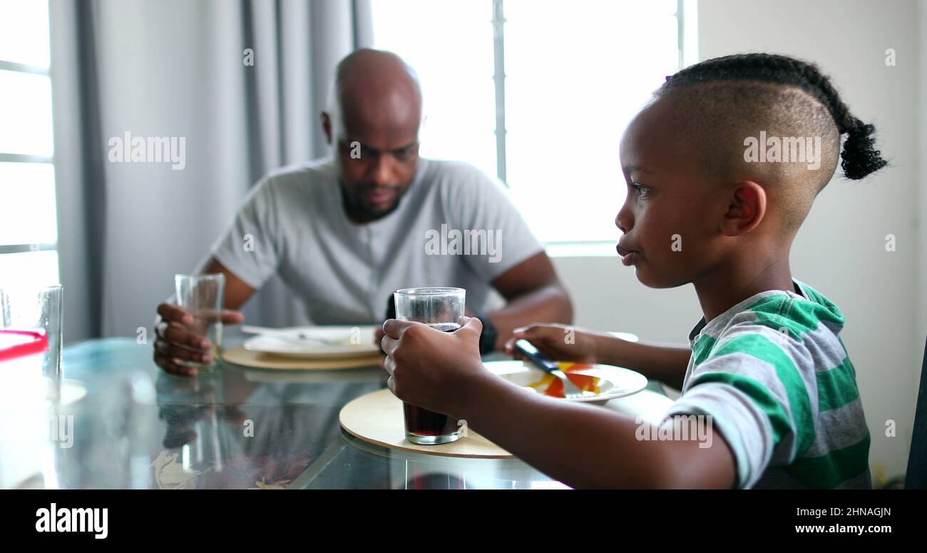 Candid black African family eating lunch, dad putting away phone, child ...