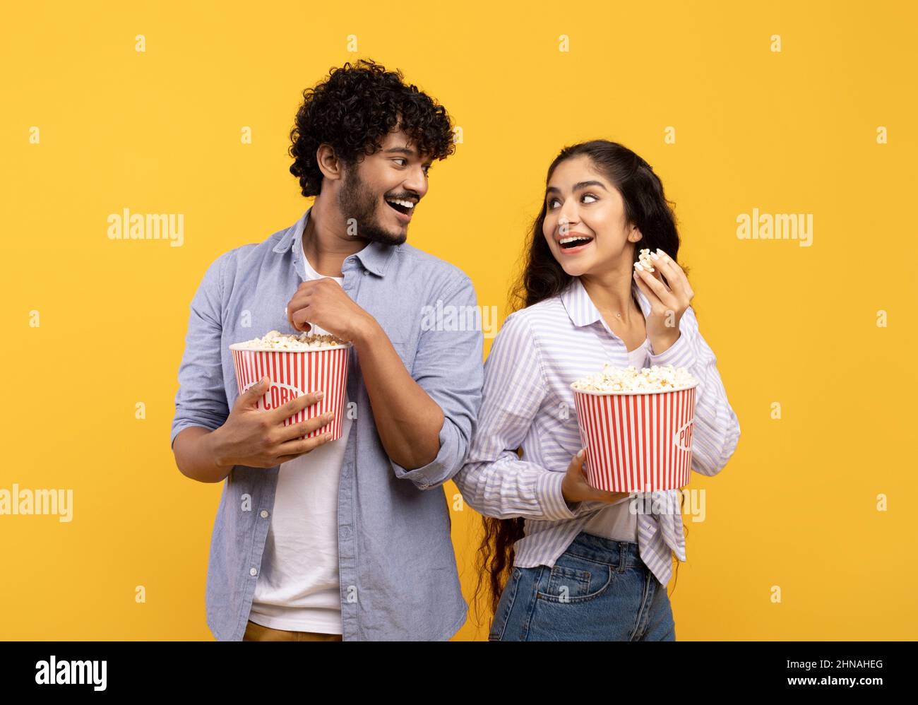 Overjoyed indian man and woman eating popcorn, standing back to back ...