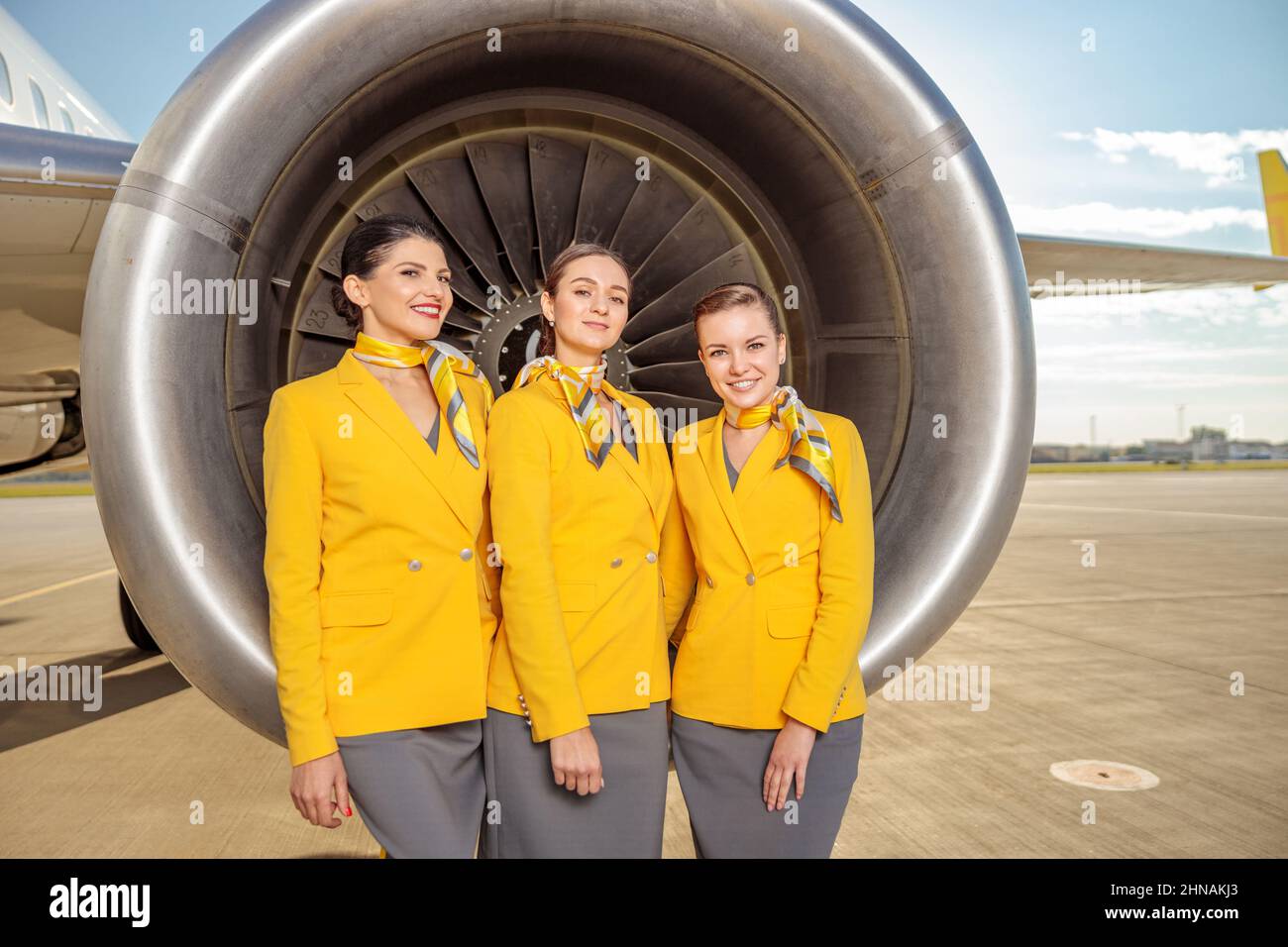 Cheerful women stewardesses standing near aircraft engine Stock Photo ...
