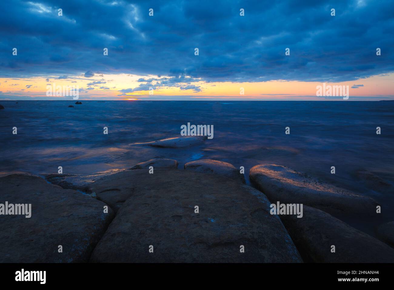 Rocky shore with stones sinking in the sea water. Sunset, long exposure ...