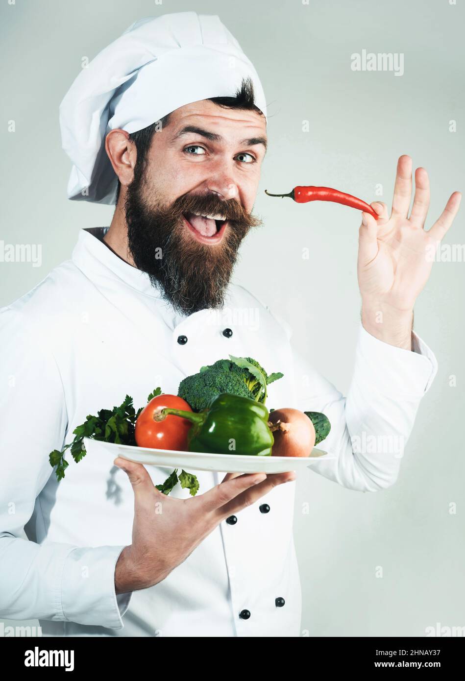 Chef in uniform with chili pepper and plate with vegetables in hands ...