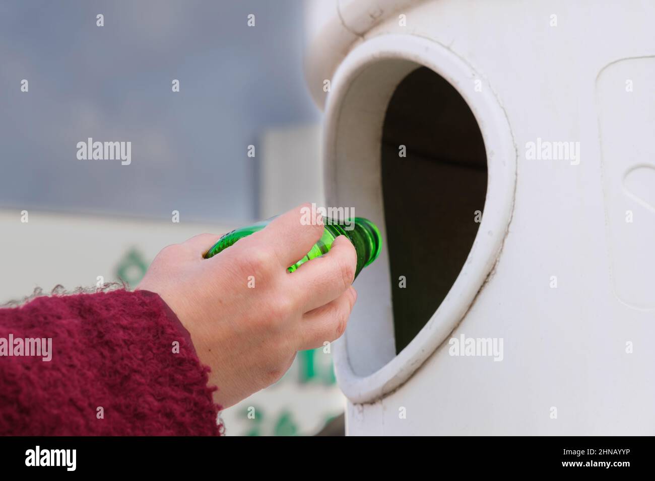 Woman or female hand throwing empty green glass bottle into recycle bin garbage container ...