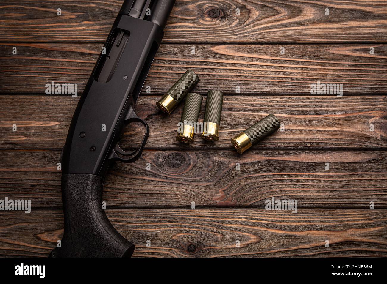 A black 12-gauge pump-action shotgun and ammo are on a wooden table. A ...