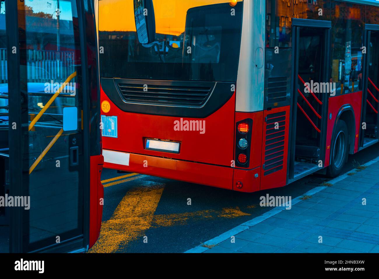 Two red bus on buses stop at city street on evening time of the day ...