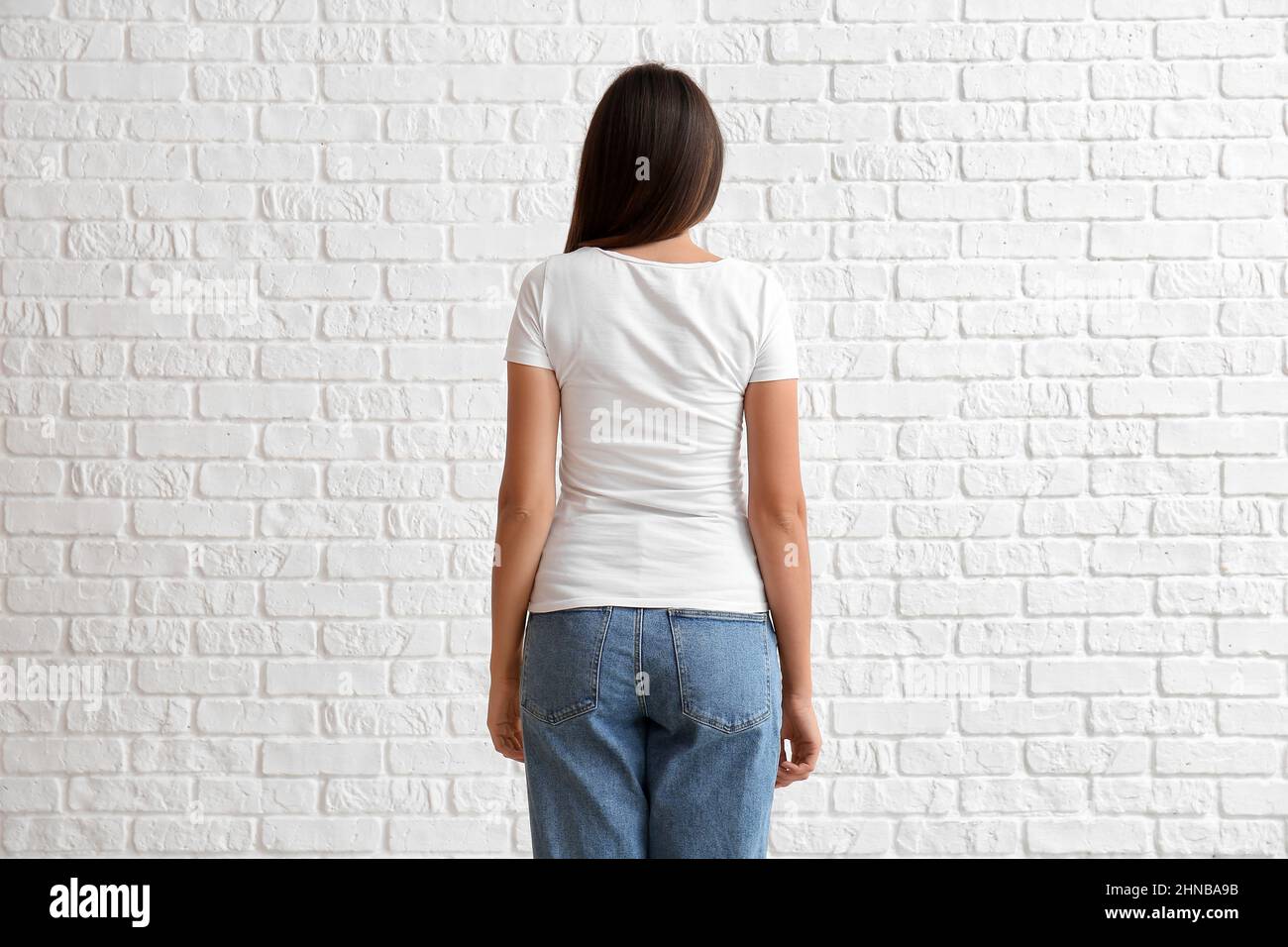 Young woman in blank t-shirt on white brick background, back view Stock ...