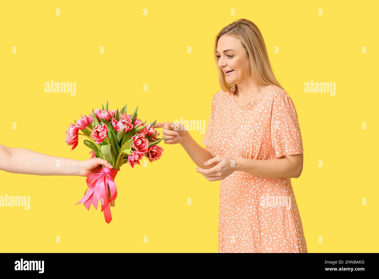 Beautiful woman receiving bouquet of flowers on yellow background ...