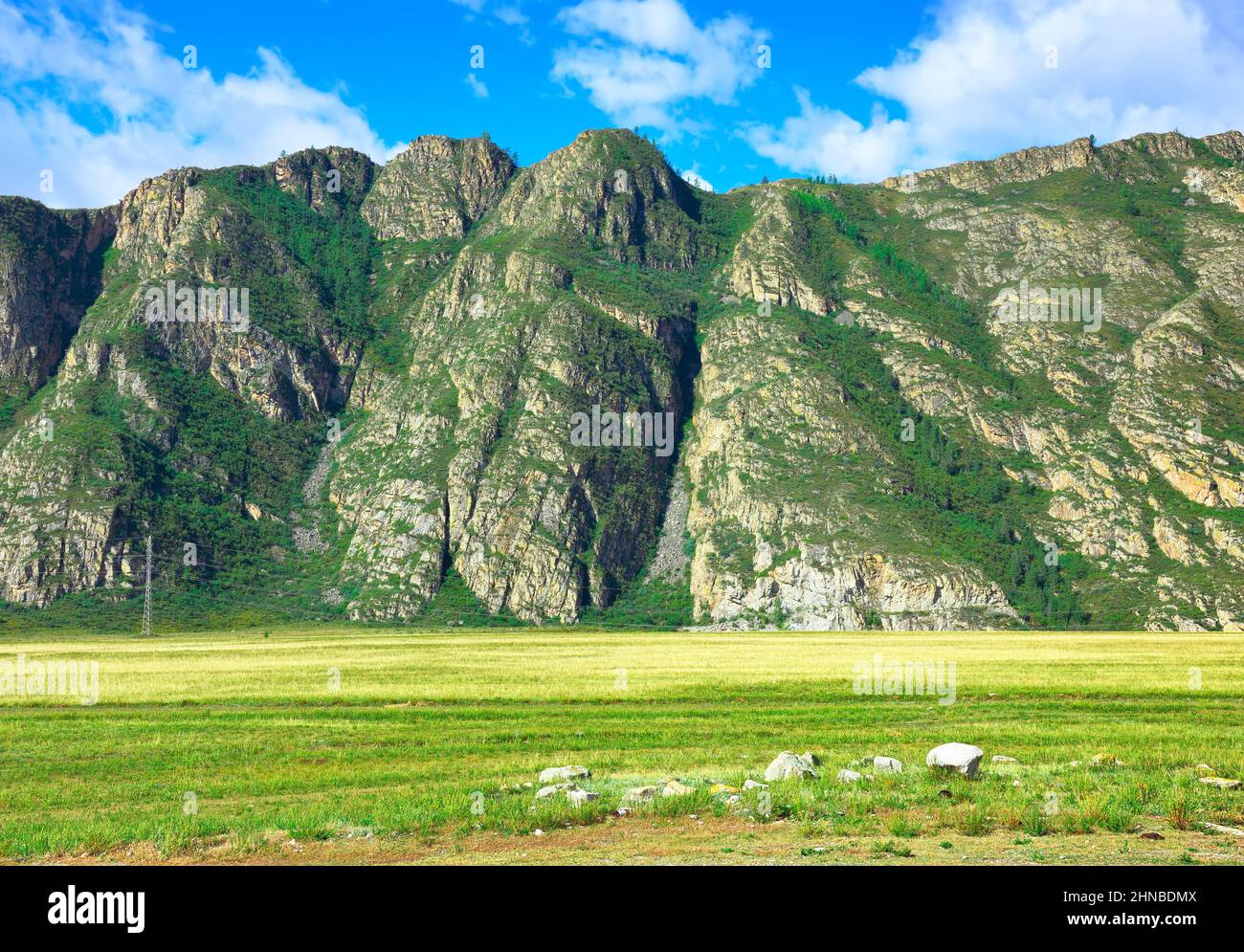 Grass at the foot of high cliffs under a blue sky. Siberia, Russia ...