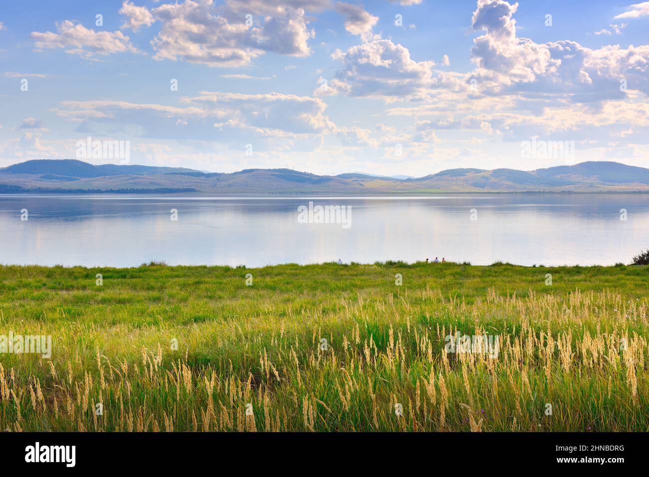 The shore of a steppe reservoir among blue mountains in summer under a blue cloudy sky. Siberia ...