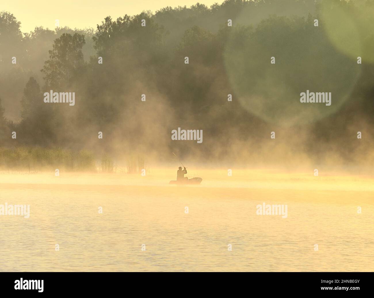 Morning on the shore of a forest lake, a fisherman on an inflatable ...