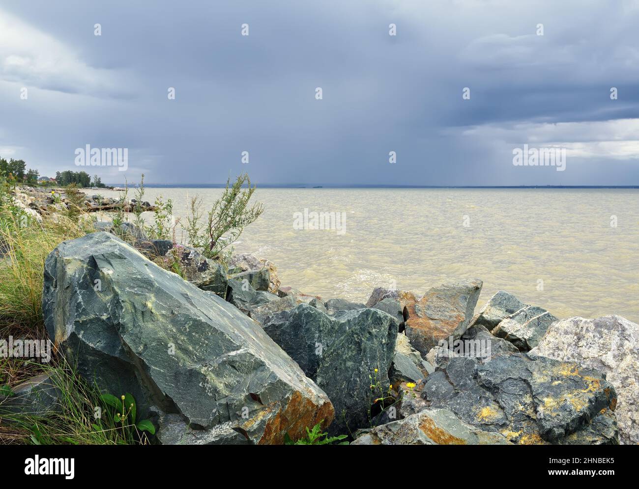 Large stones on the shore of the Ob sea, waves on the water under a ...