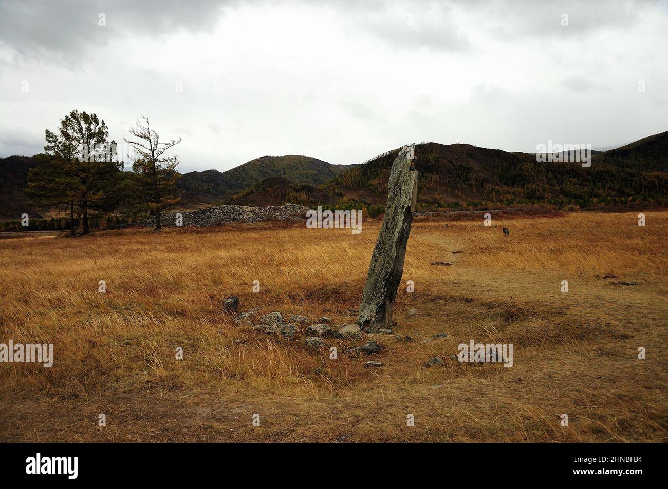 An ancient gravestone in an autumn valley at the foot of a mountain ...