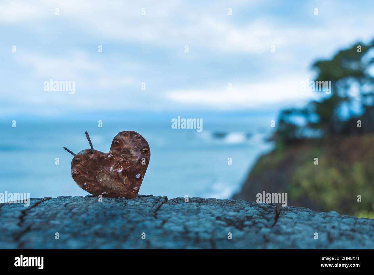 Closeup of a metal heart shape on a cliff with the sea under a cloudy ...