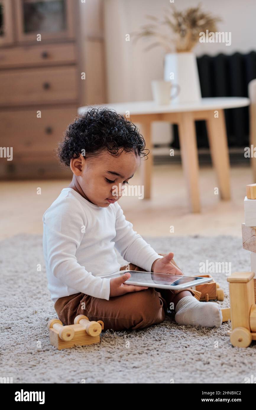 Concentrated curly black boy sitting on carpet in living room and ...