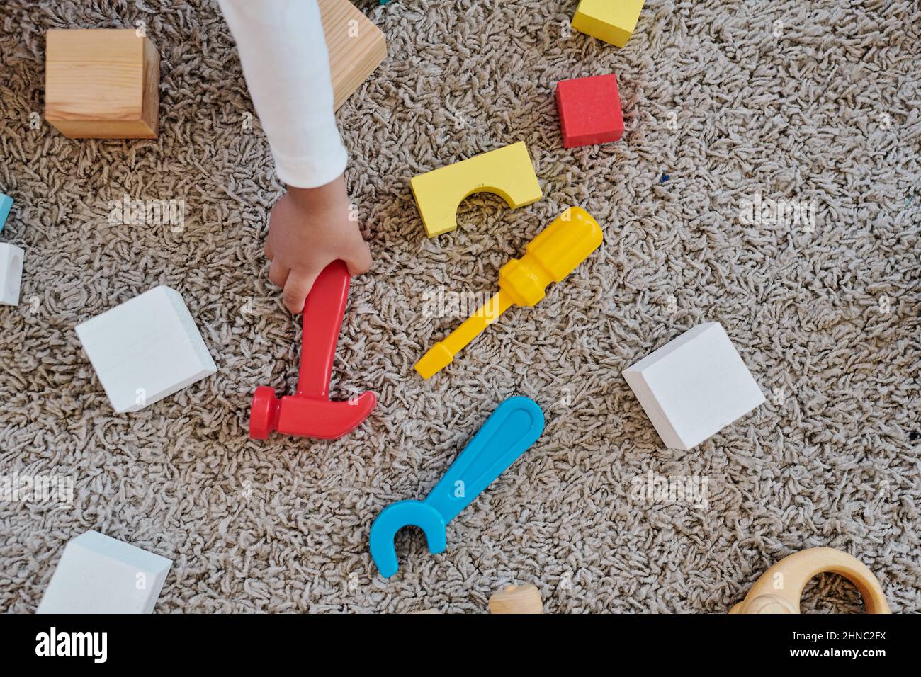 Above view of unrecognizable toddler taking toy hammer from carpet ...