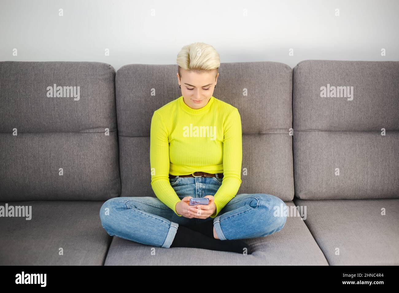 Tomboy woman typing message on mobile phone while sitting on couch at ...