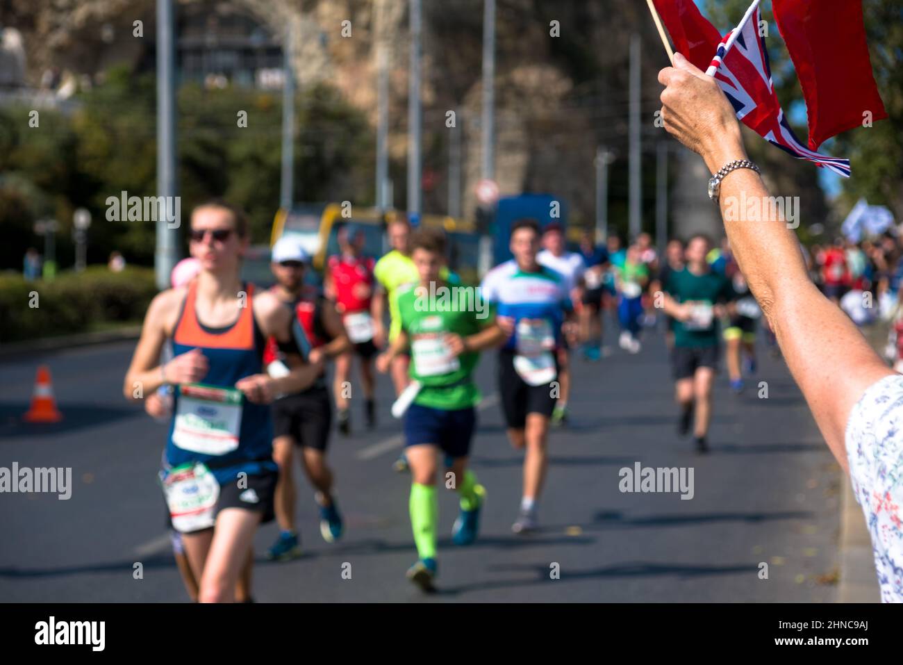 Hand holding flags against unfocused marathon runners Stock Photo - Alamy