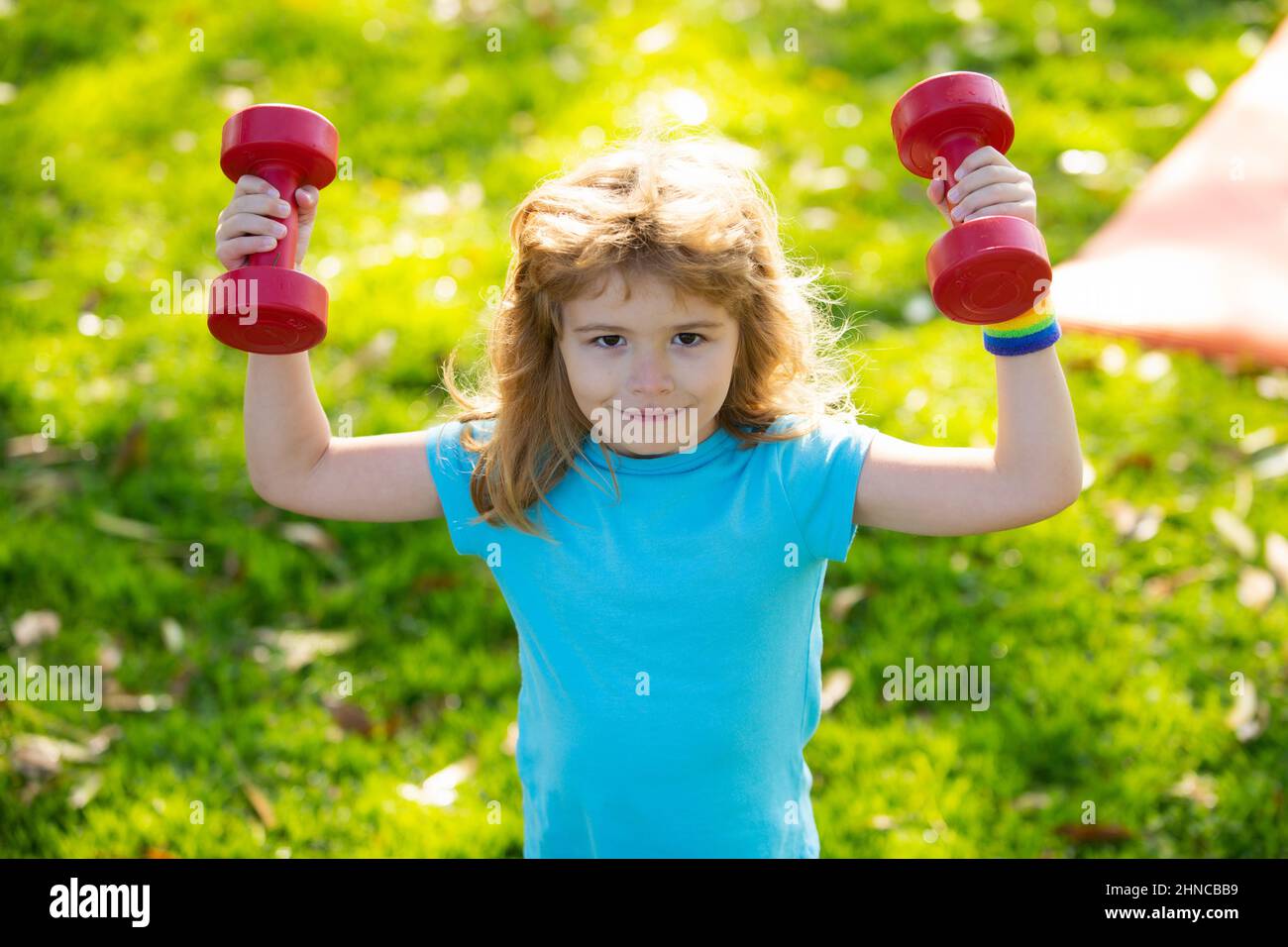 Cute little boy doing exercises with dumbbells in green park. Portrait ...