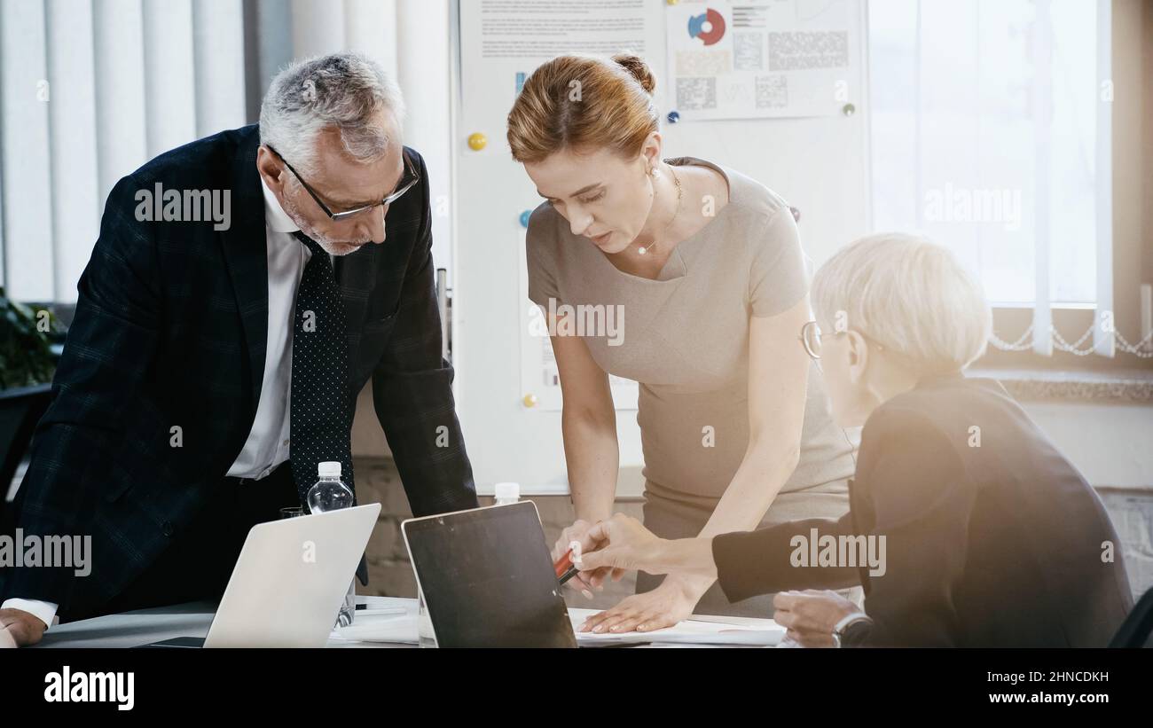 Business people looking at documents near colleague pointing at laptop ...