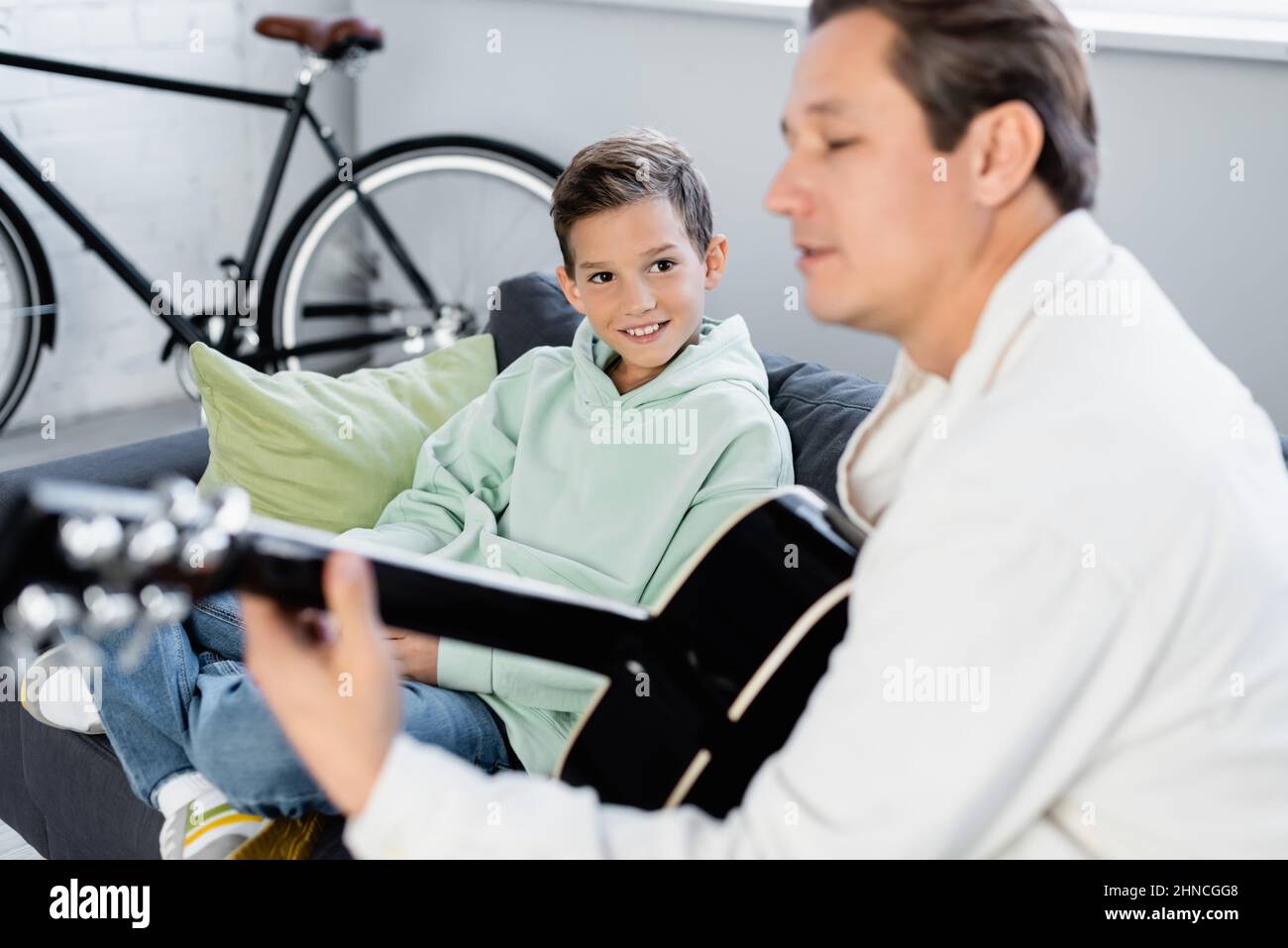 Smiling preteen kid looking at blurred dad playing acoustic guitar at ...
