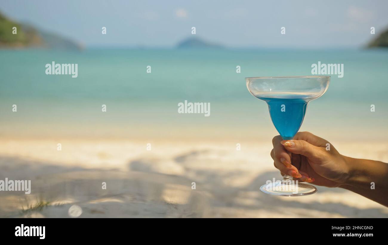 Woman hands shake blue cocktails in wineglasses resting on beach in ...