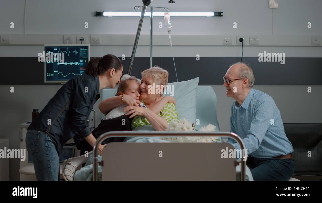Niece and daughter visiting sick grandma in hospital ward bed, bringing ...