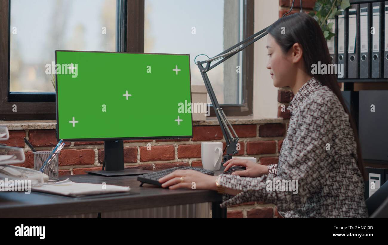 Asian woman working on monitor with horizontal green screen in startup ...