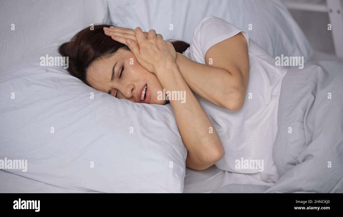 woman with closed eyes covering ear with hands while suffering from ...