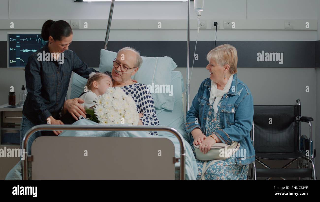 Family visiting old patient and bringing flowers in hospital ward bed ...