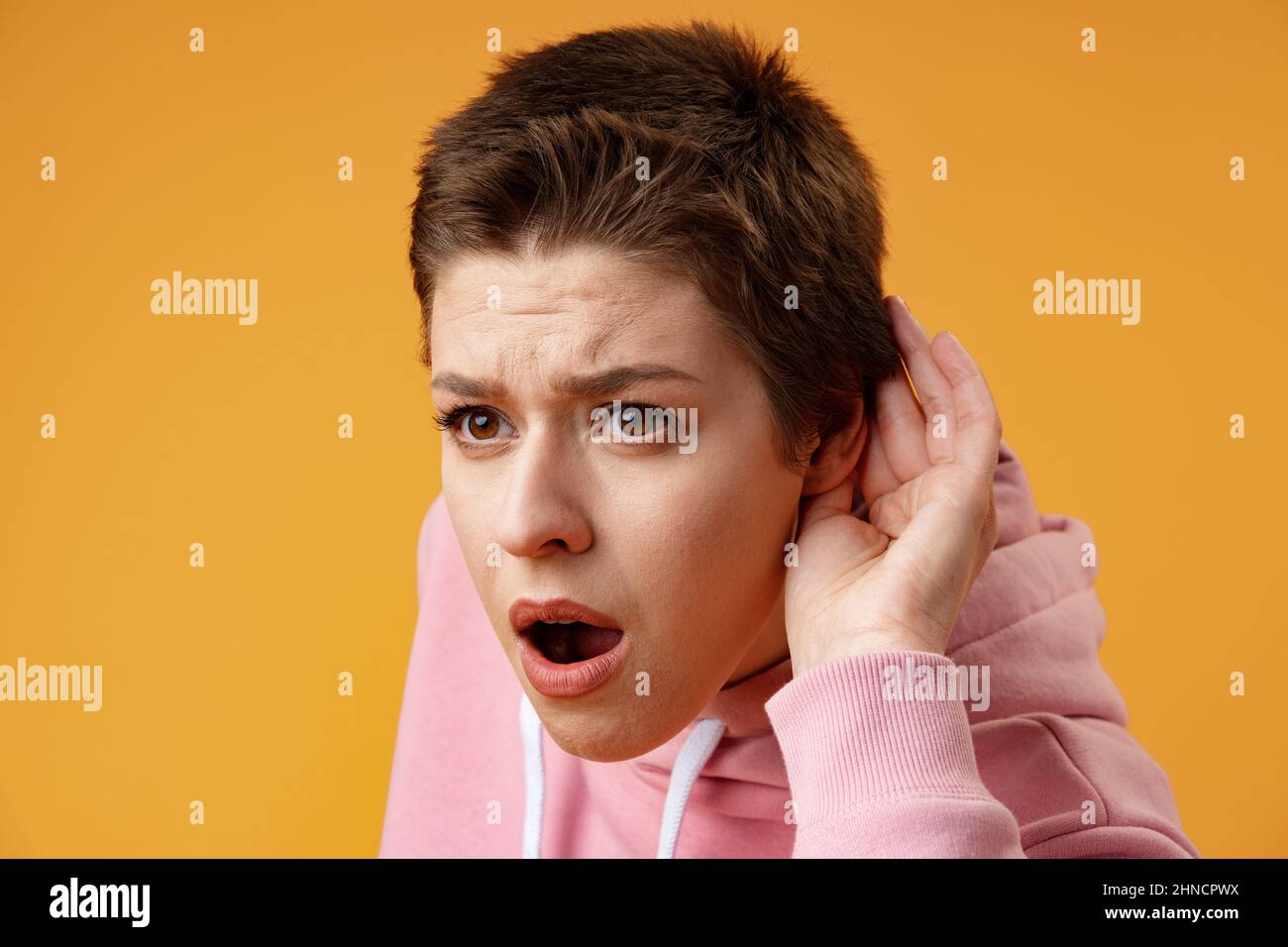 Young girl doing listen gesture with hand on ear over yellow background ...