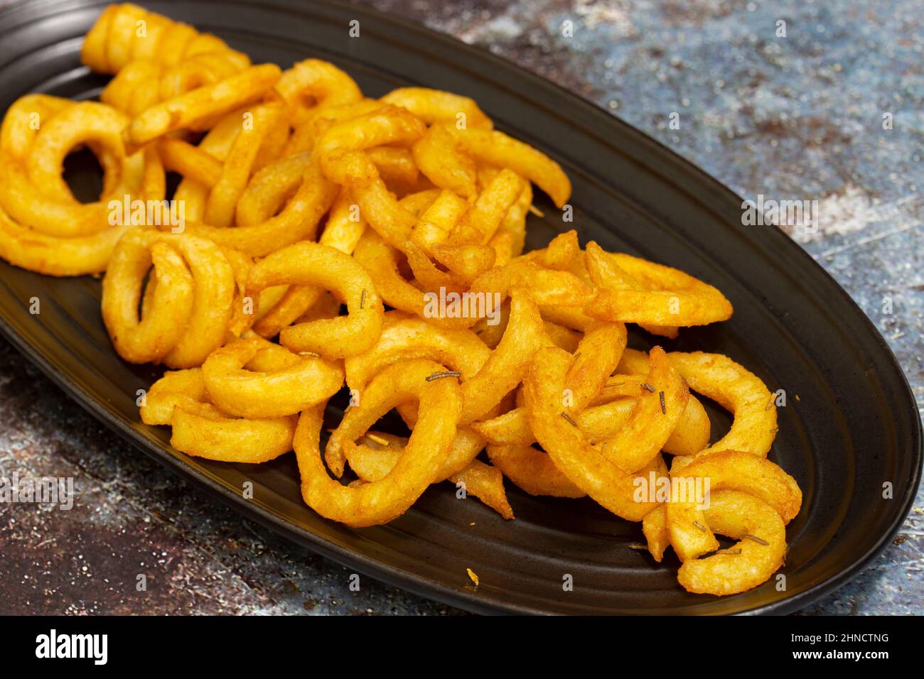 Spicy seasoned curly fries on a black stoneware oval plate. Fast food ...