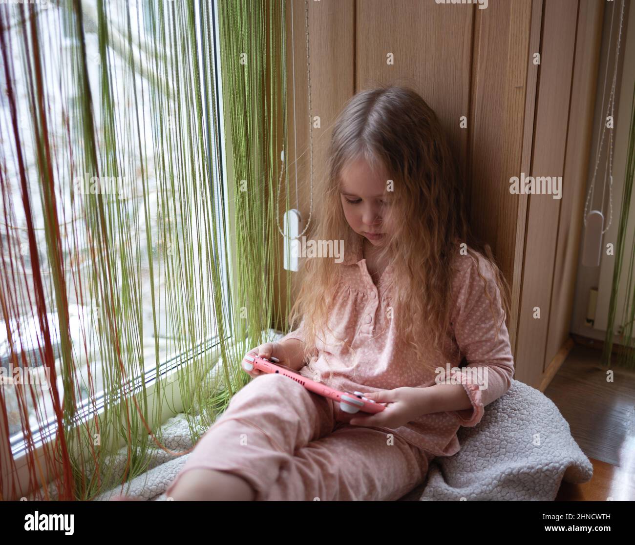little cute girl plays a game console sitting on the windowsill Stock ...
