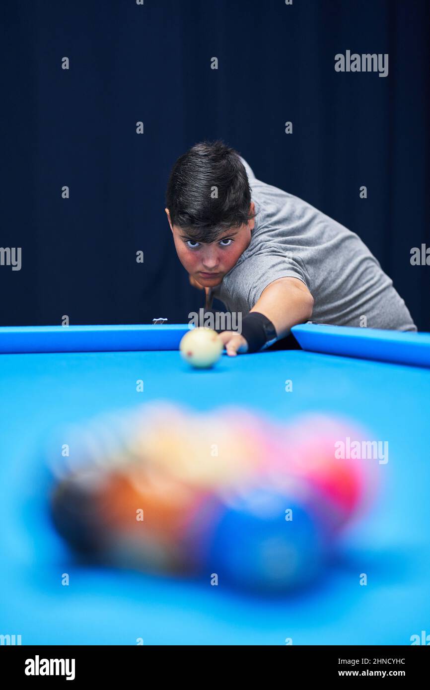 Serious boy in casual wear with cue stick preparing to hit ball while ...