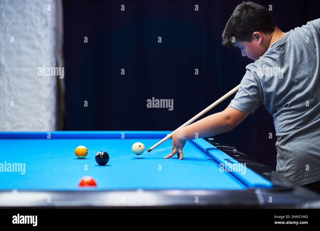 Side view of serious boy in casual wear with cue stick preparing to hit ...