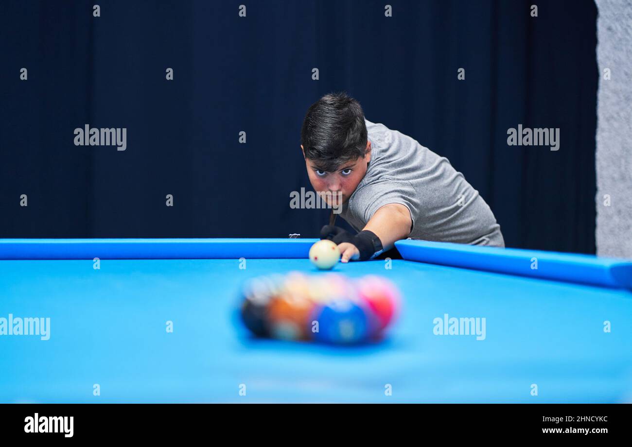 Serious boy in casual wear with cue stick preparing to hit ball while ...