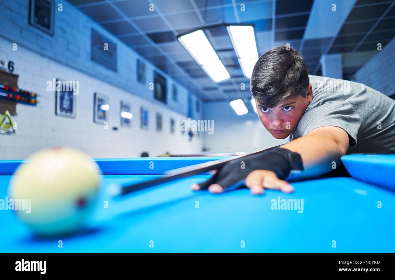 Serious boy in casual wear with cue stick preparing to hit ball while ...