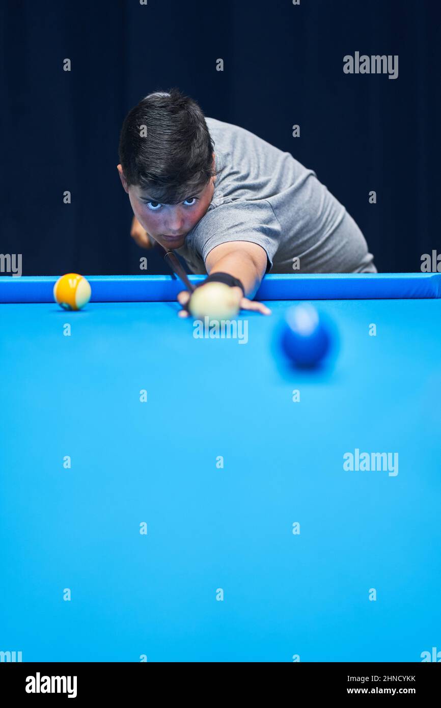 Serious boy in casual wear with cue stick preparing to hit ball while ...