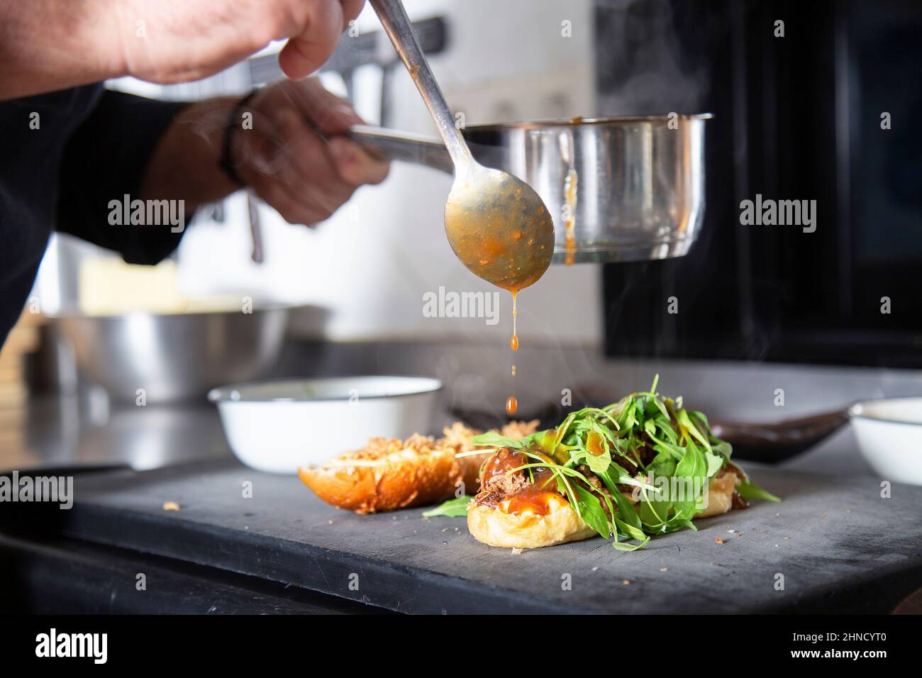 Crop anonymous chef pouring tasty sauce on bun of sandwich with meat ...